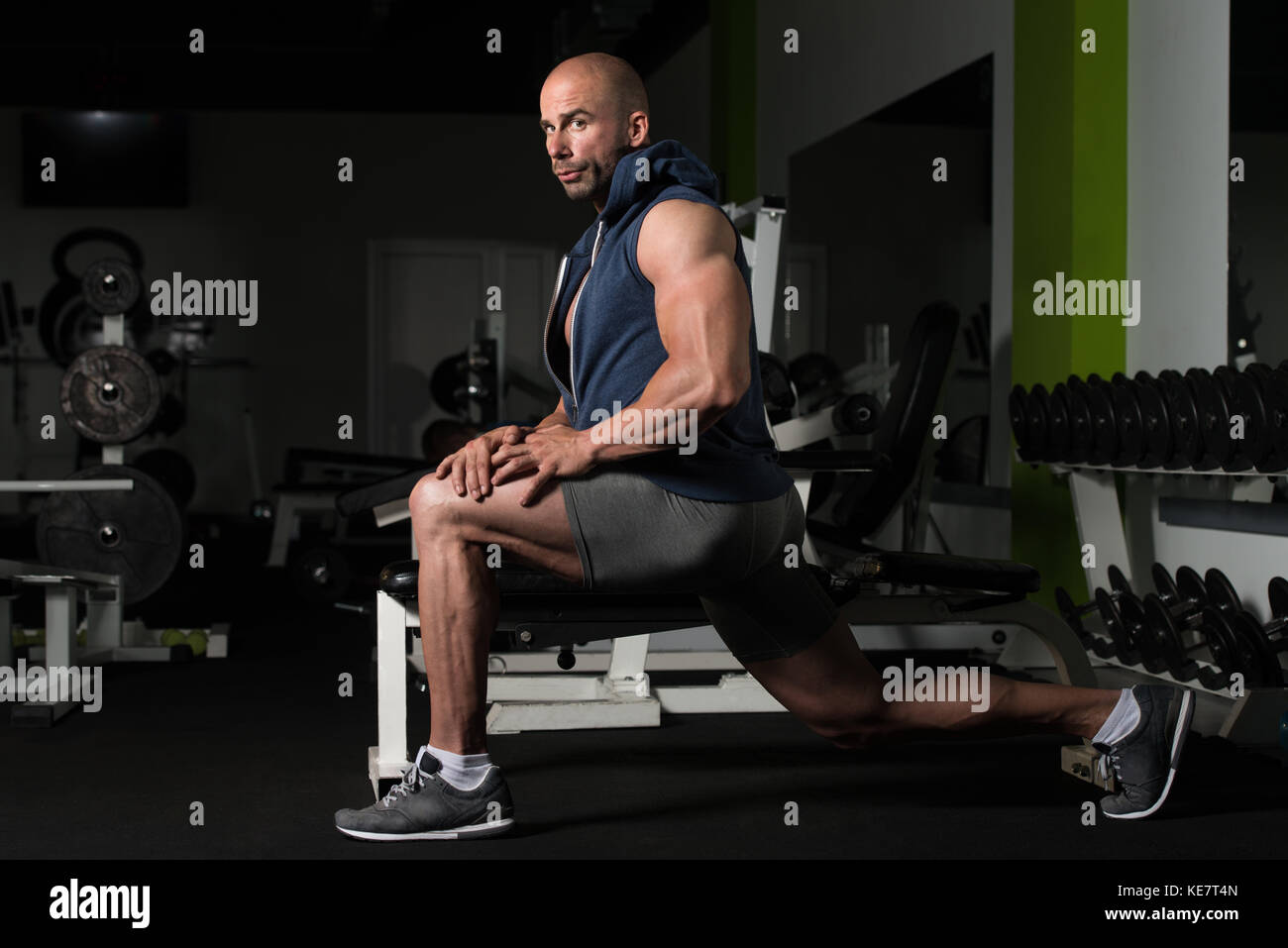 Muscular Man Stretching His Leg At The Floor In A Gym And Flexing ...