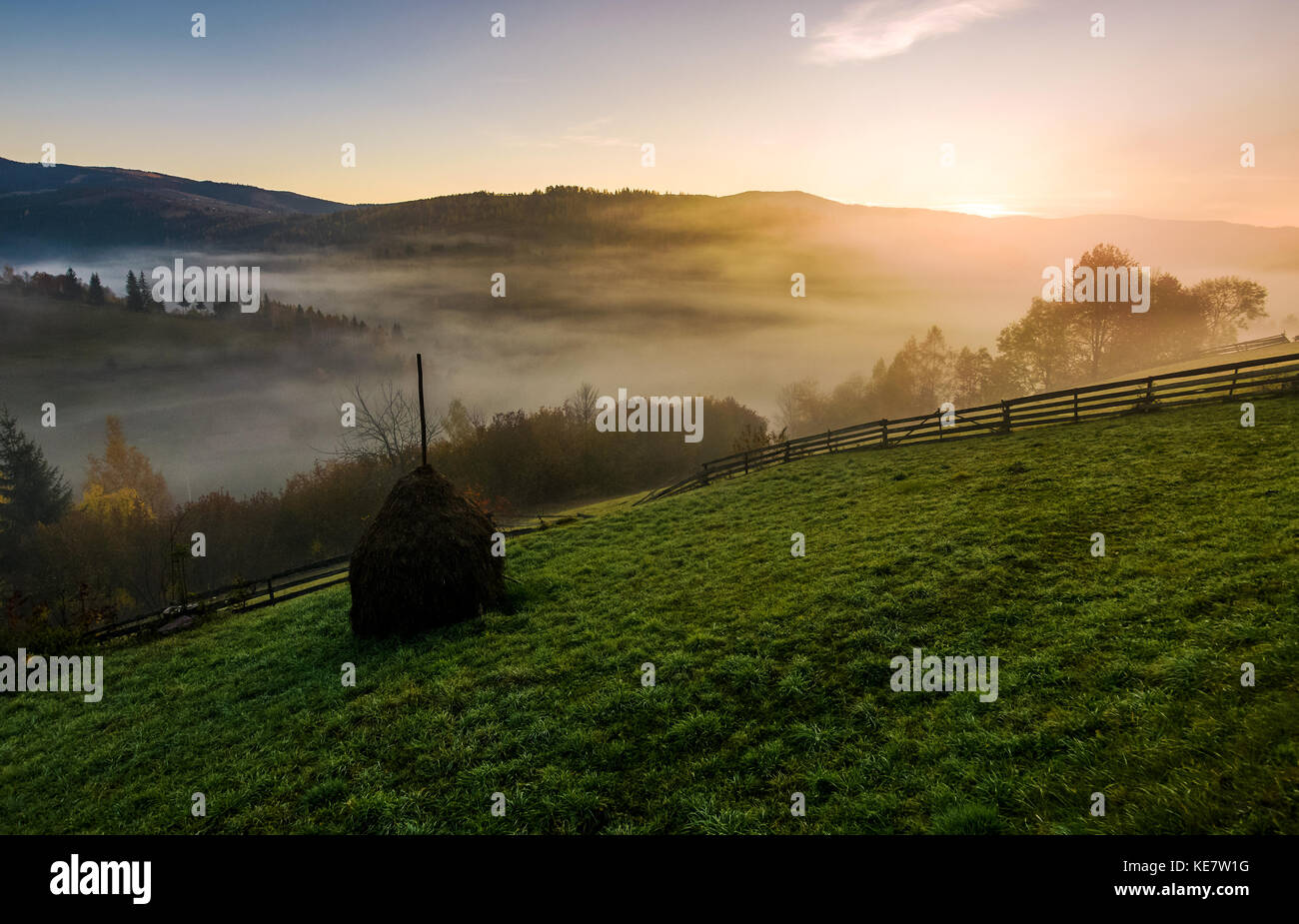 haystack and wooden fence on hillside at foggy autumn morning in ...