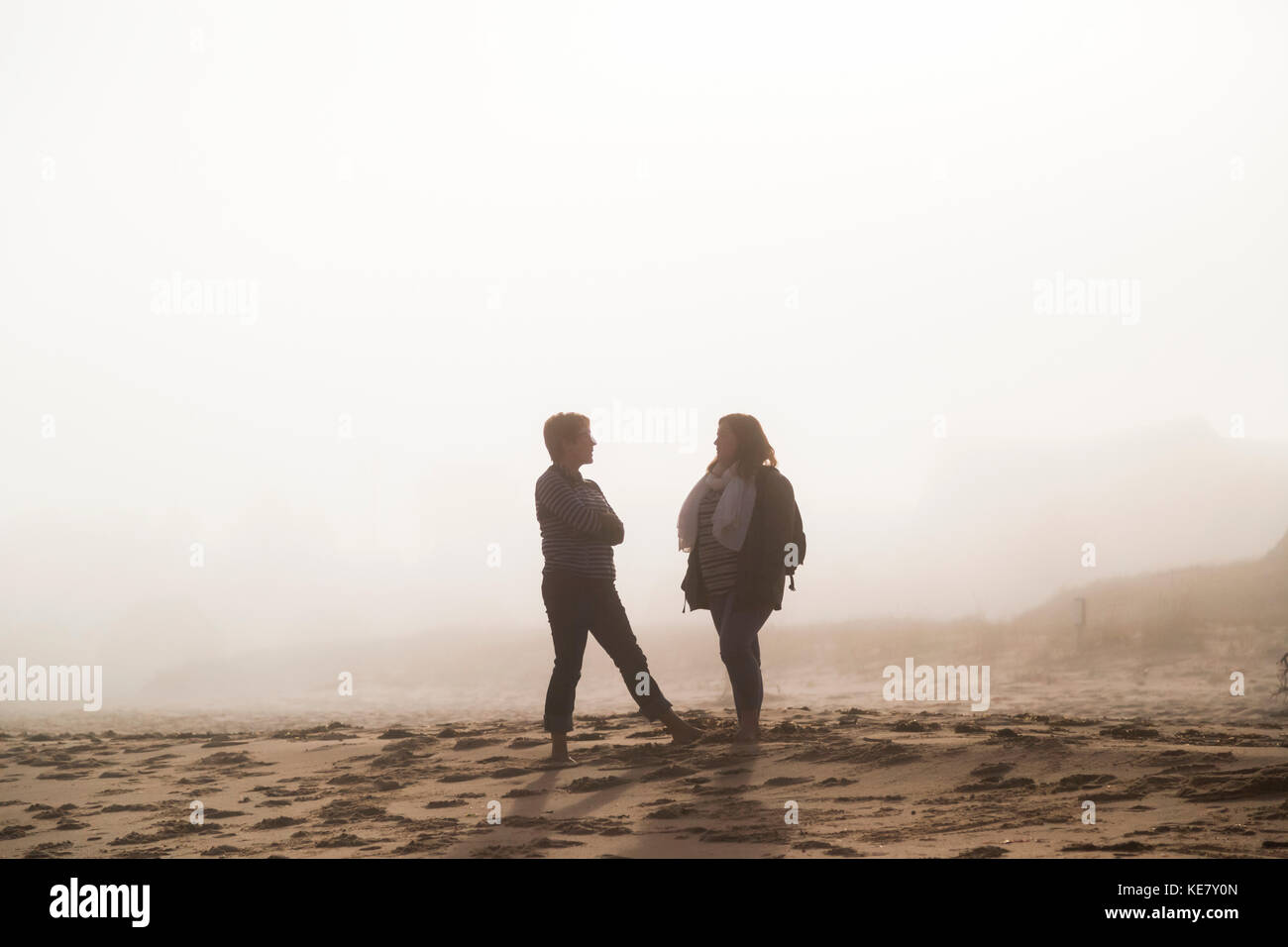 Two Female Friends Stand Talking On A Beach In The Mist; Prince Edward ...