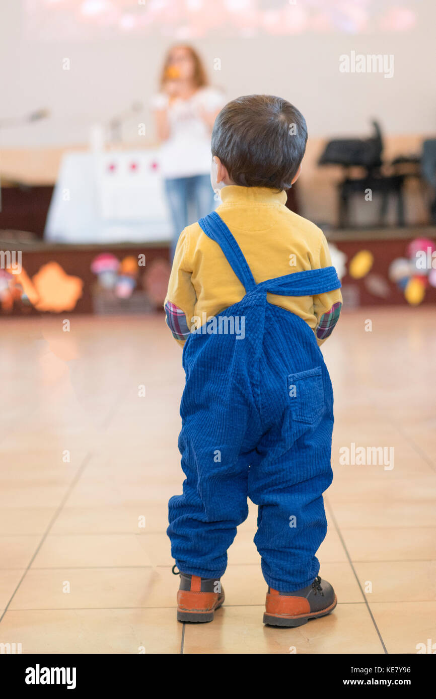 A little handsome boy in blue pants is standing in the concert hall ...