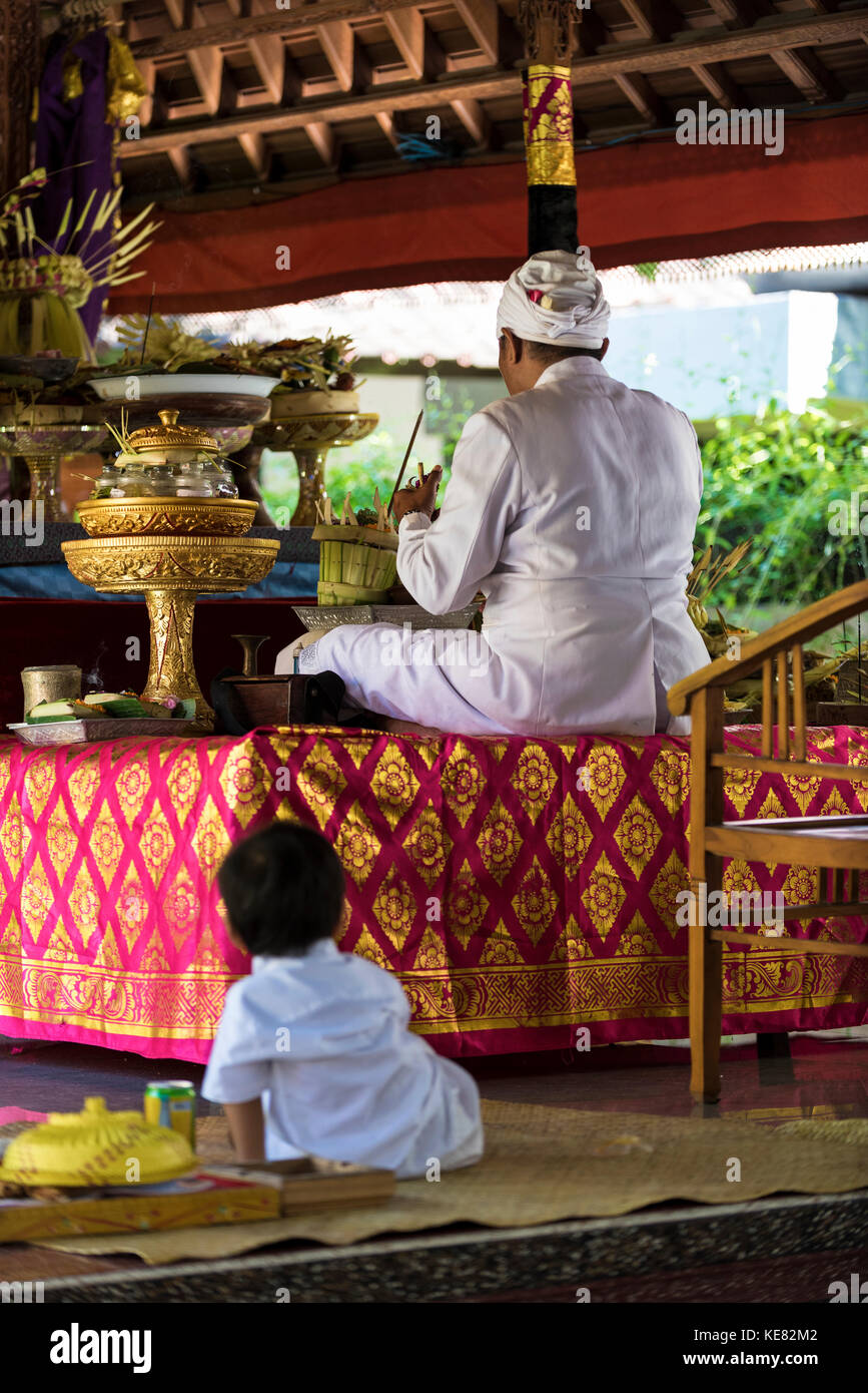 A Young Boy Sits Watching A Man Perform A Religious Ceremony; Bali ...