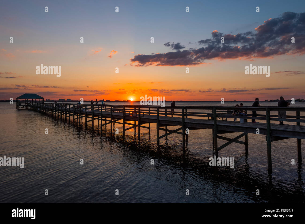 People standing on a pier as the sun sets over the Indian River ...