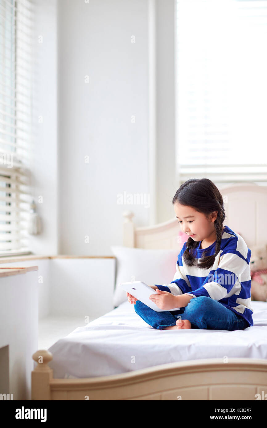 Girl using electric tablet sitting on bed Stock Photo - Alamy