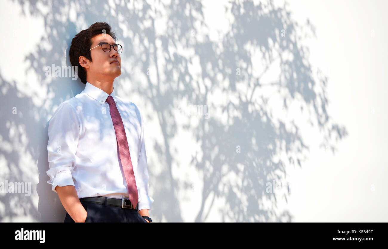 Businessman relaxing leaning against a wall Stock Photo - Alamy