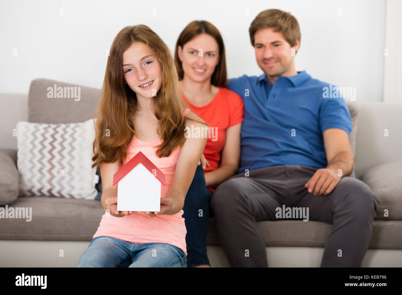 Smiling Girl Holding Small House Model In Front Of Her Parent Sitting ...
