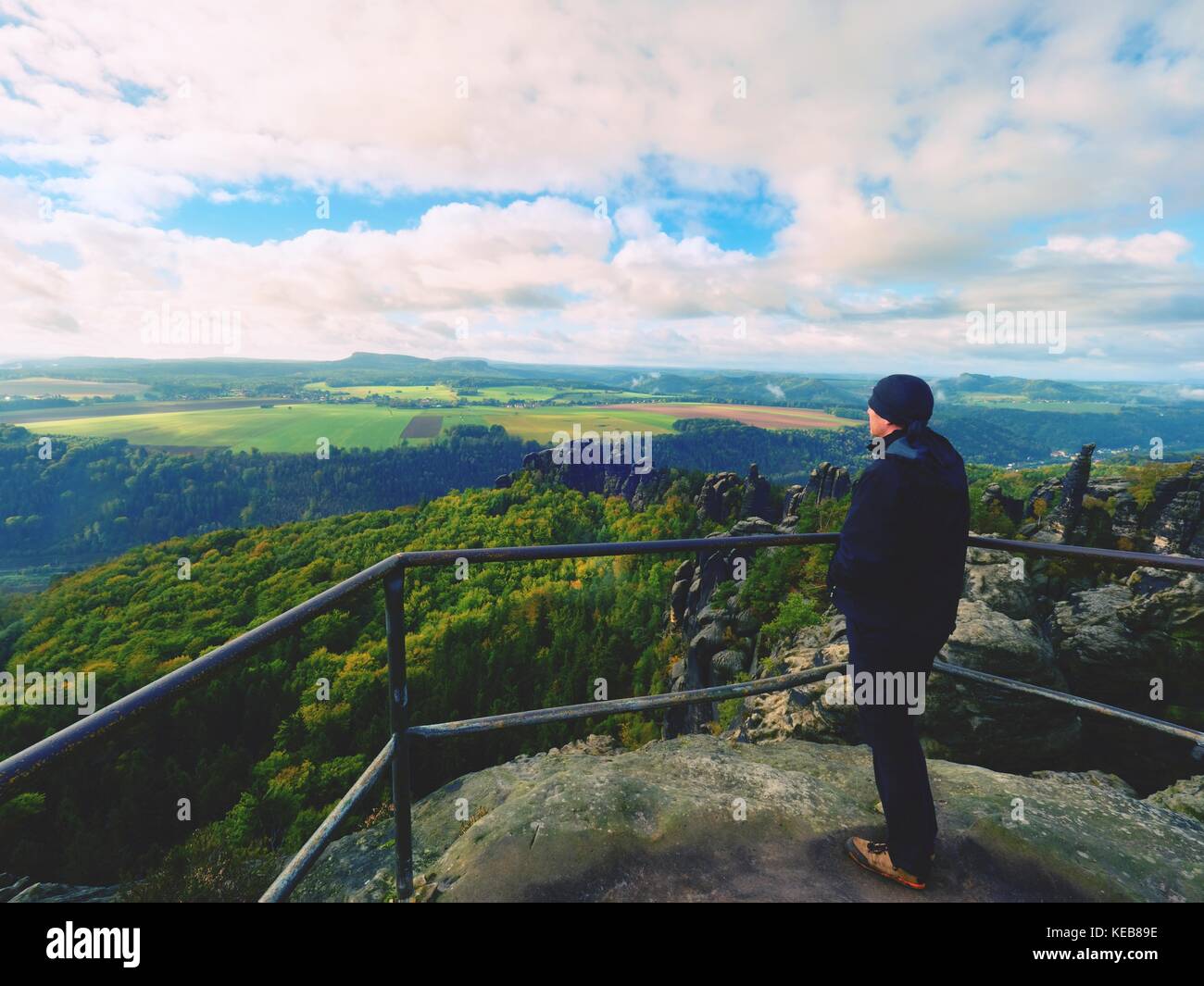 Man hiker at handrail on the peak of sandstone rock watching into misty ...
