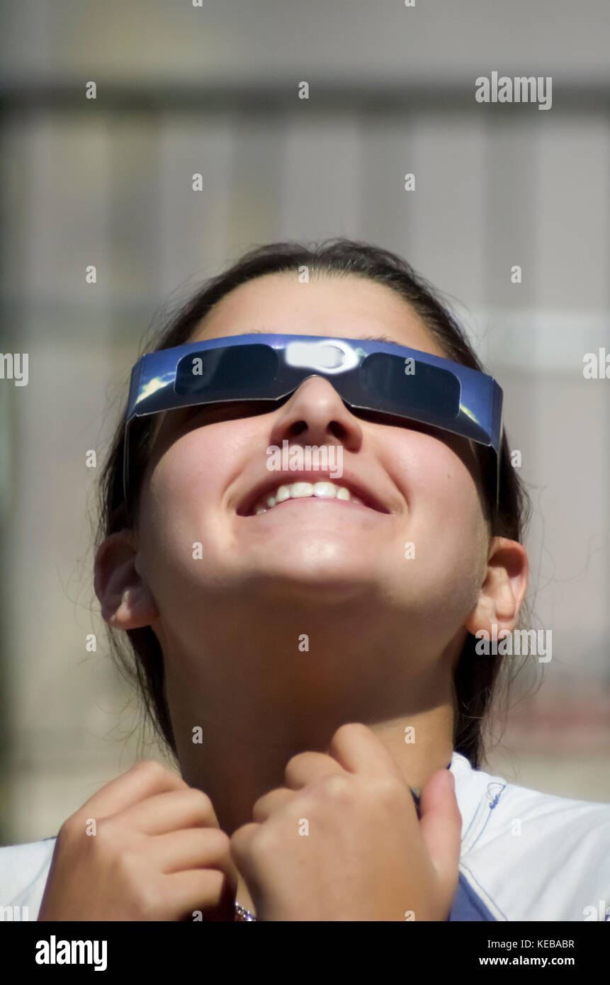 a smiling young student, looking at the sun with special glasses ...