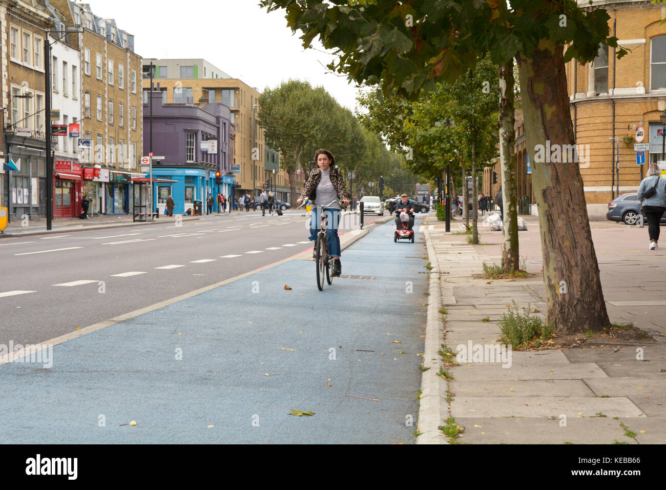 Cyclist and man on mobility scooter in cycle lane on Mile End Road in ...