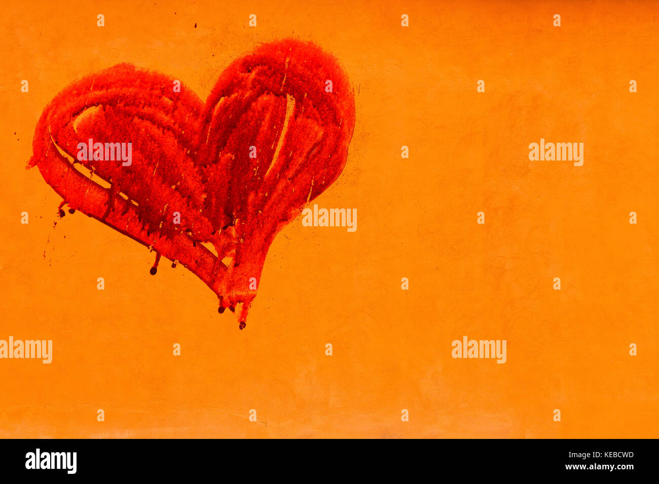Red colored heart manually painted with drips in an orange wall with ...