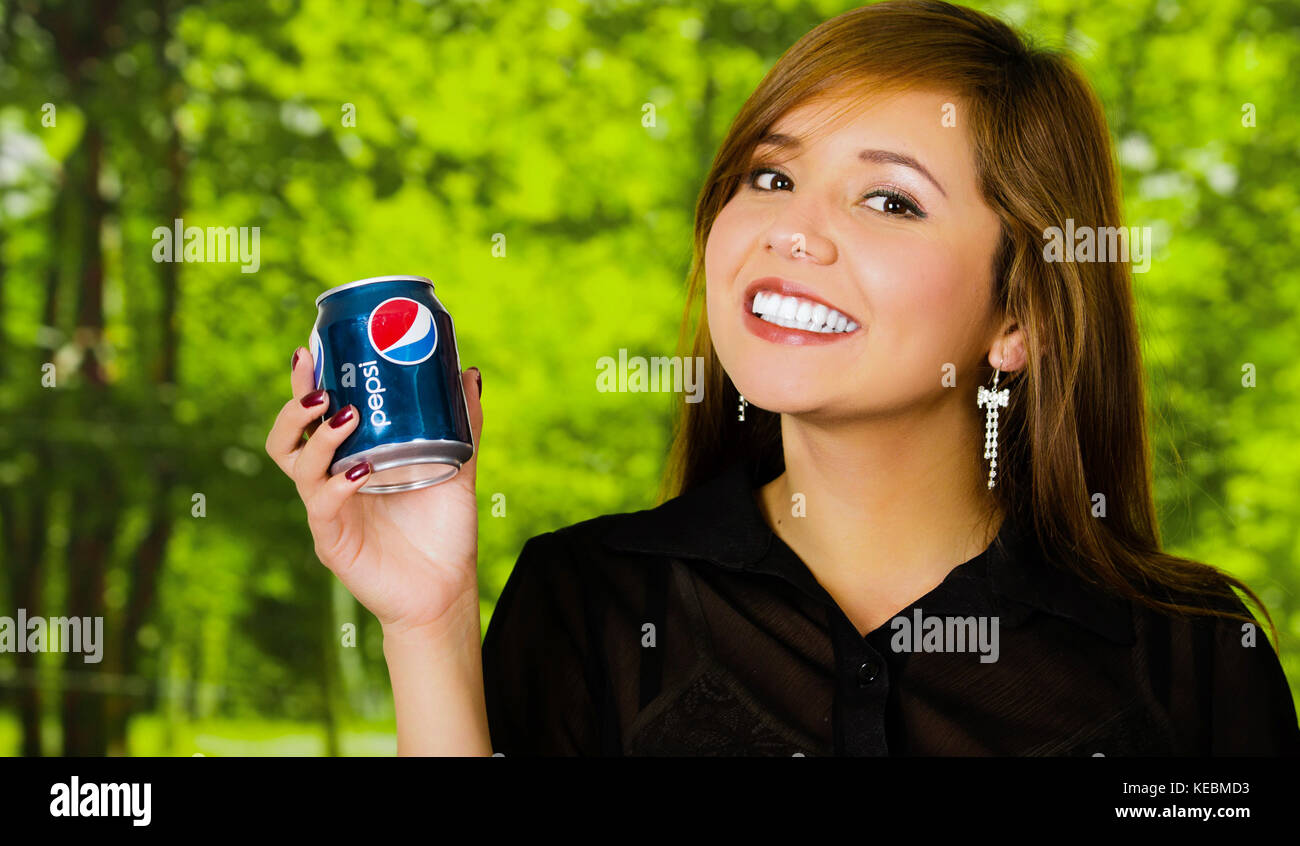 Smiling pretty young woman holding a pepsi in blurred green background ...