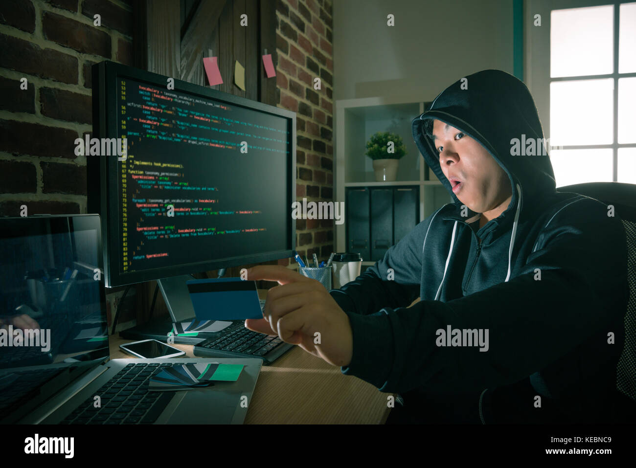 young hacker man looking at credit card feeling surprised when he ...