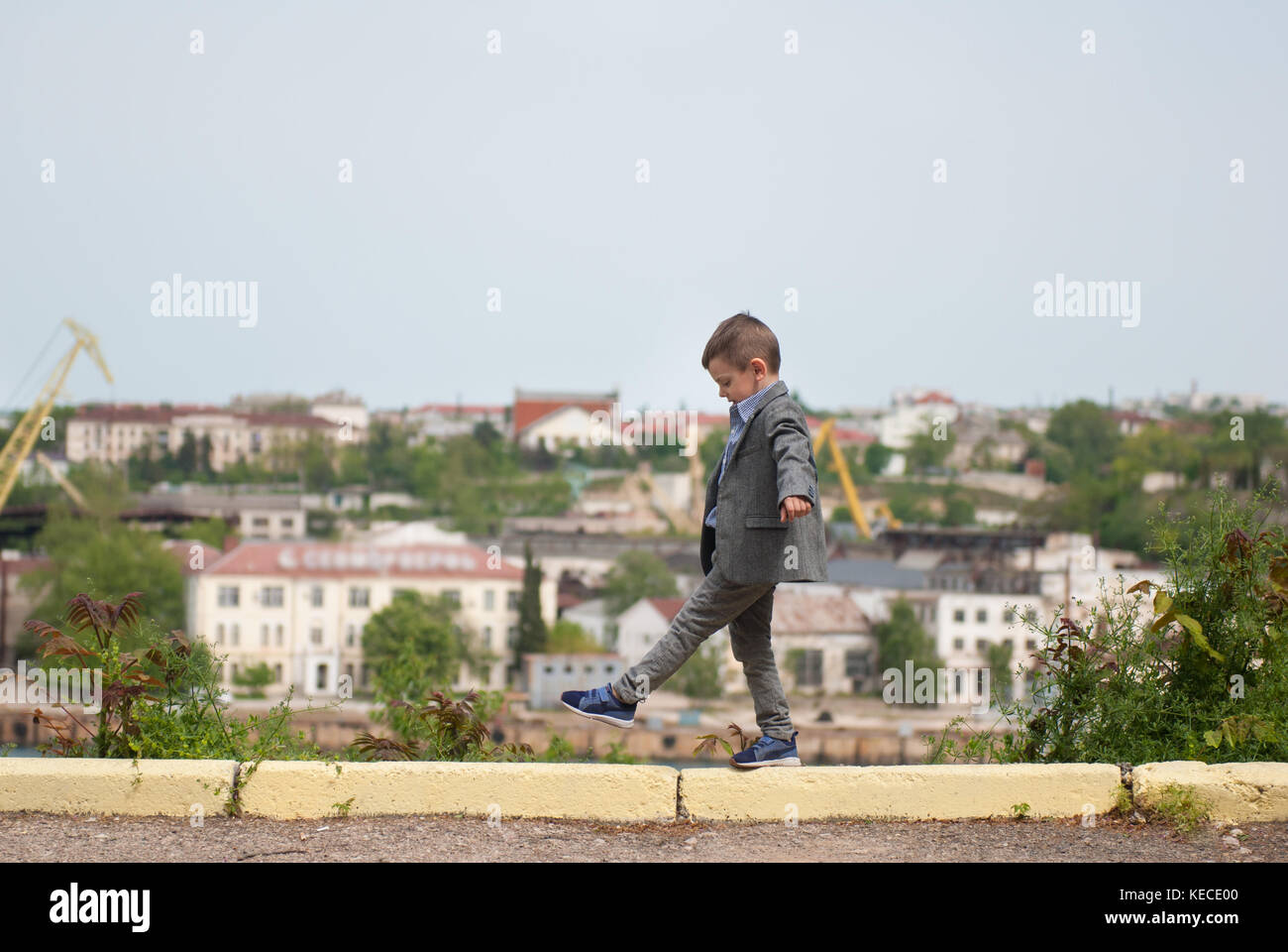 adorable little boy in jacket walking on the curb in the background of ...