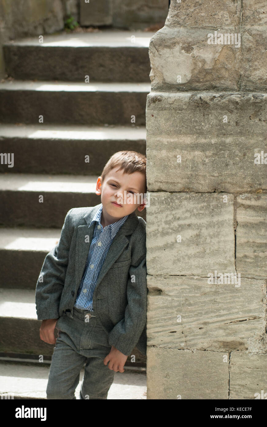 Beautiful little boy in a costume leaning on an ancient stone wall ...