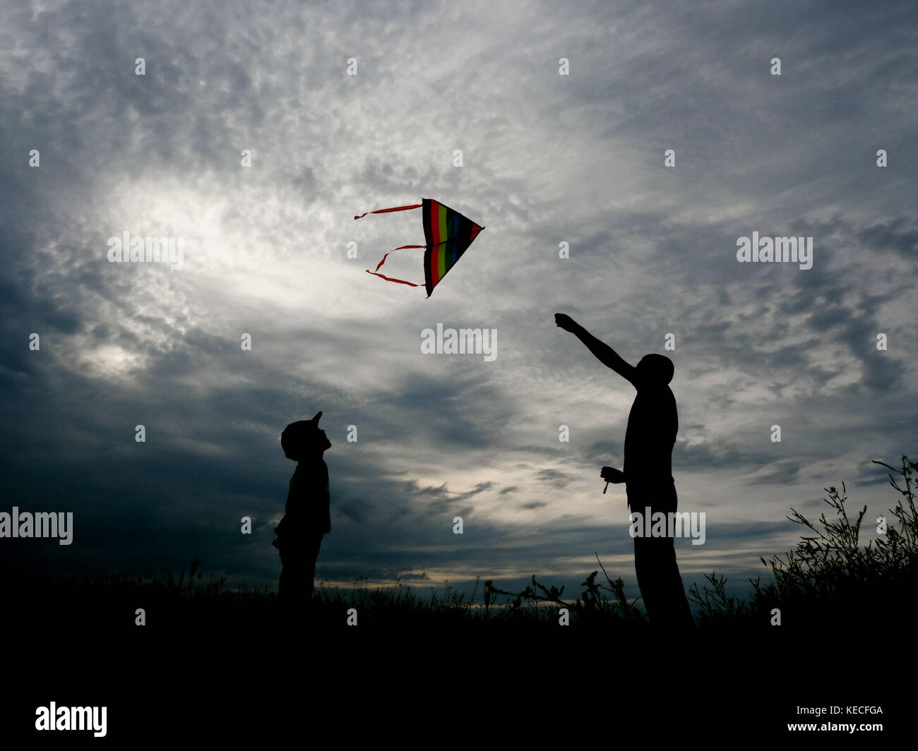 Adult man and little child launch a kite against a beautiful summer ...