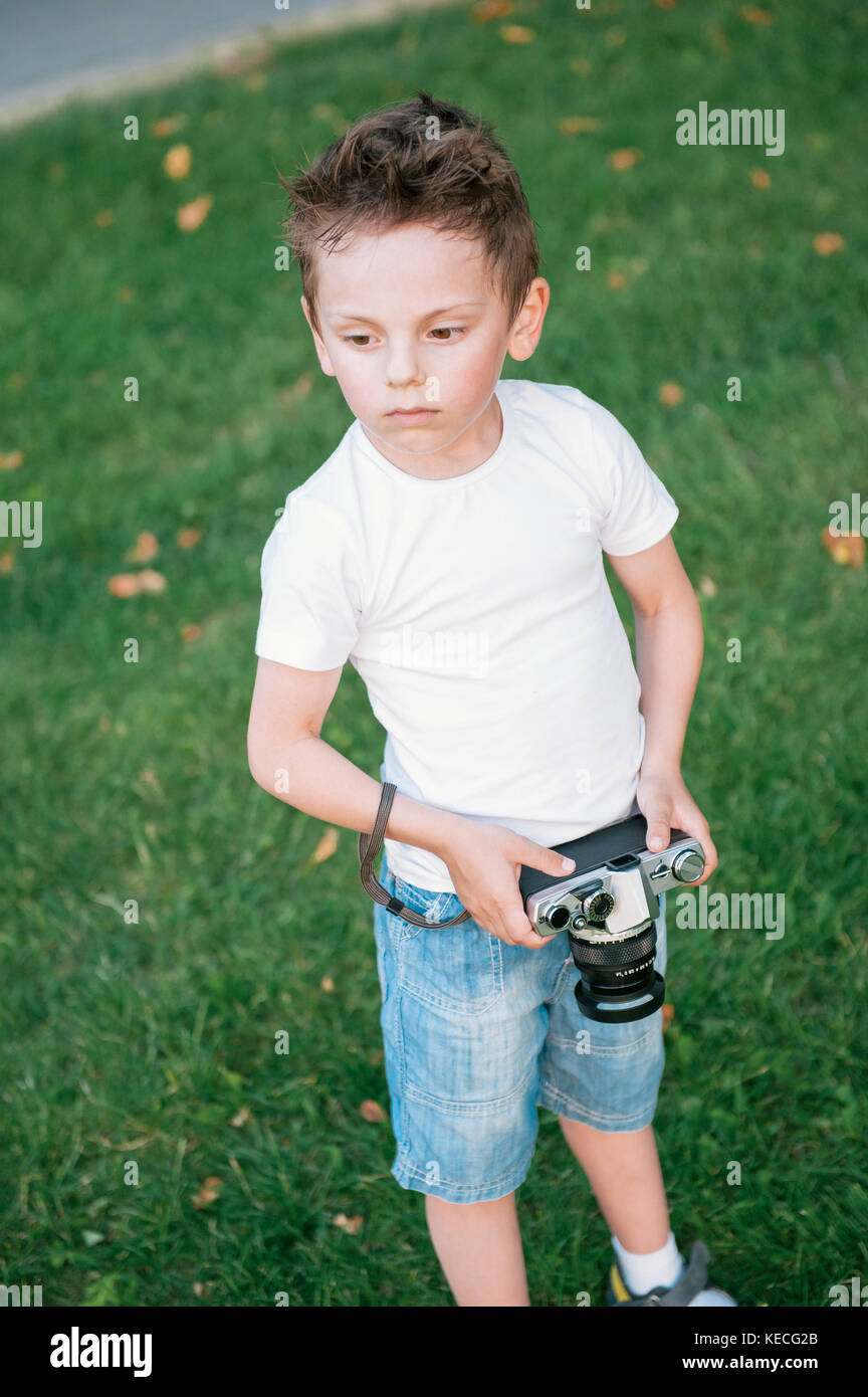 handsome kid holding film camera standing on green grass with fallen ...