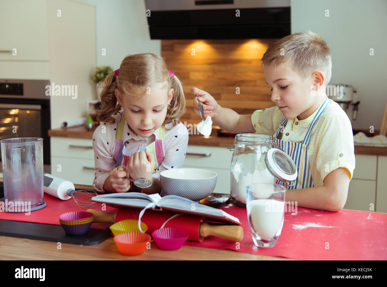 Two happy little and cute children preparing muffins at modern kitchen ...