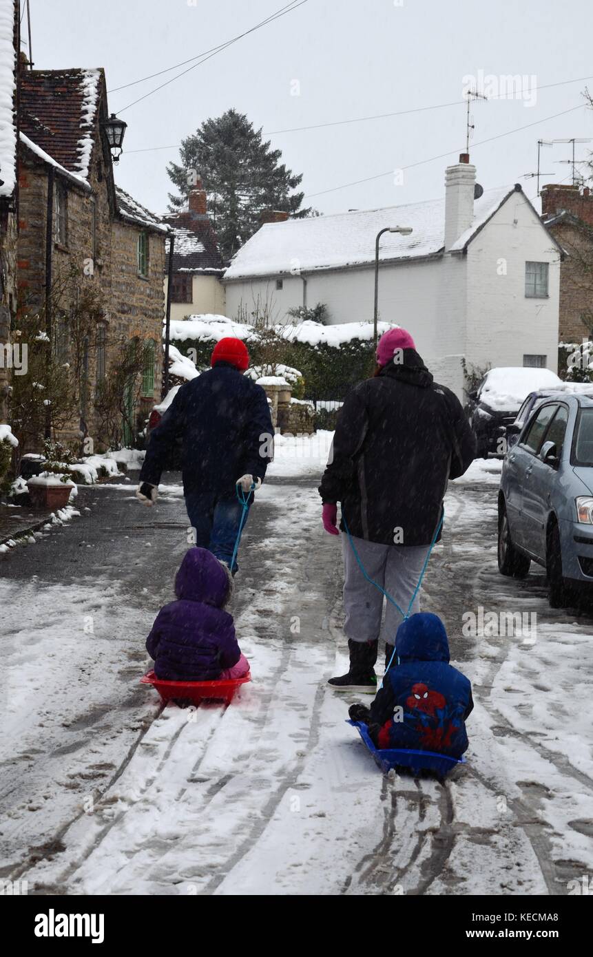 Parents pulling their children on sledges in a wintry village scene ...