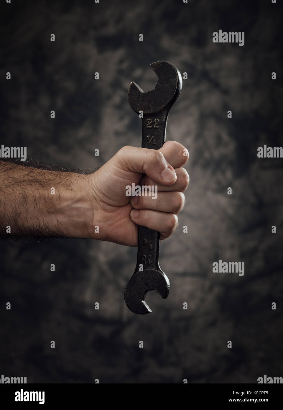 Manual worker holding a spanner on dark background, empowerment and ...