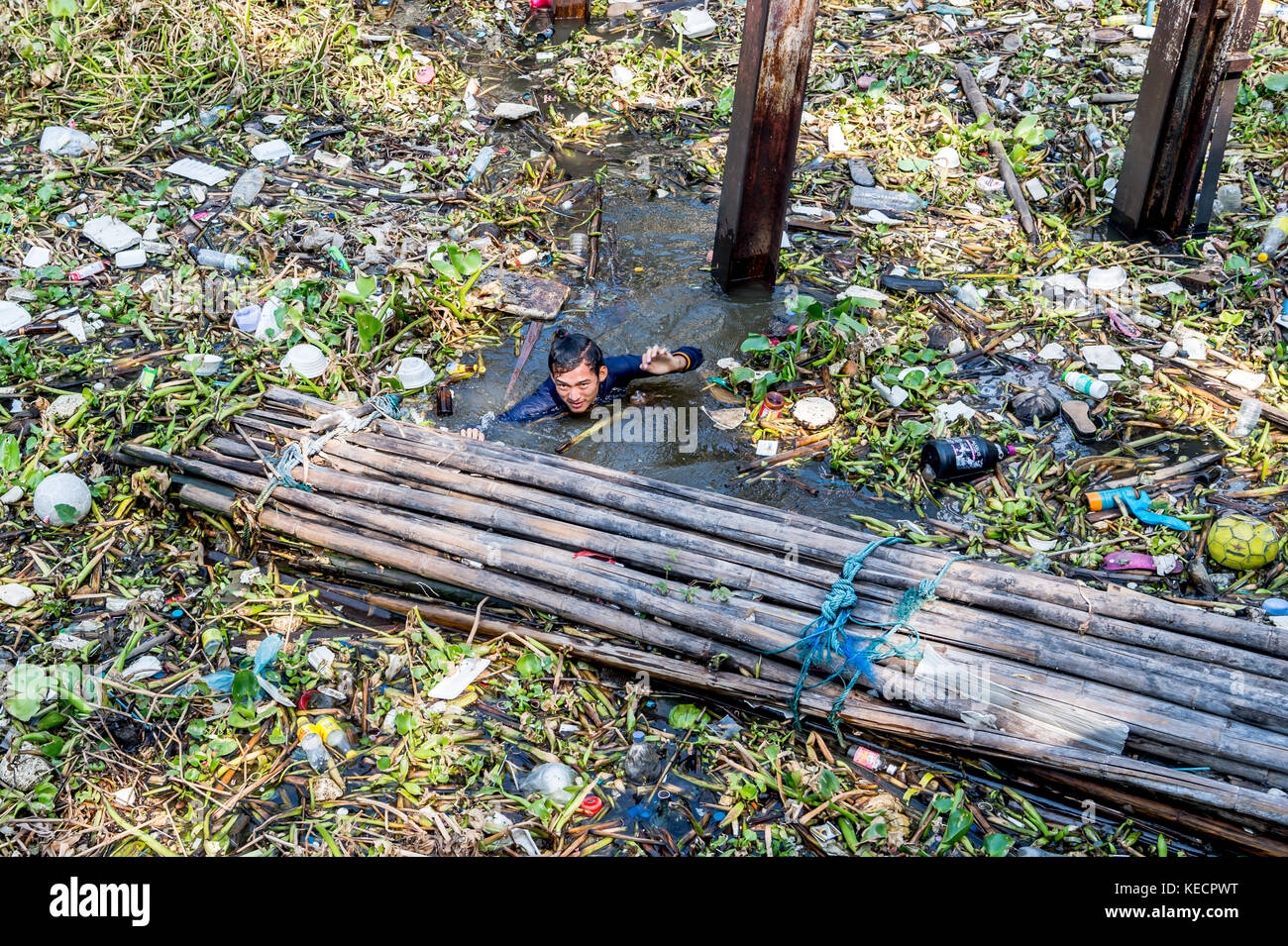 A Thai man swims amongst the rubbish, pollution and debris in a small ...