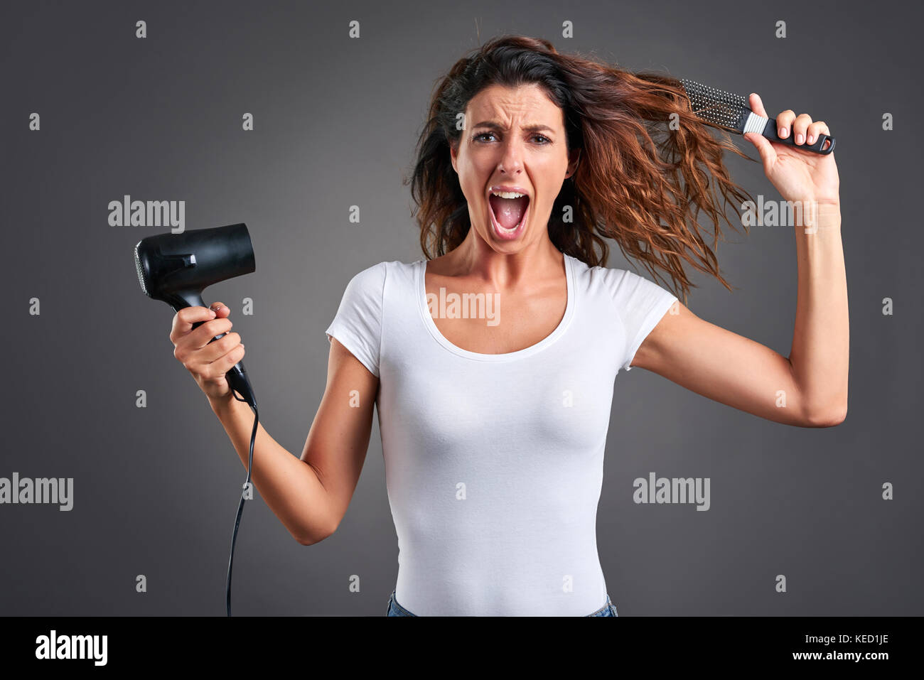 A beautiful young woman screaming while using a hairdryer and a ...