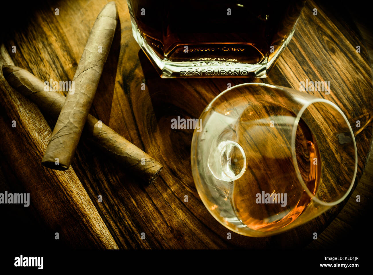 Top view of two cigars, a glass and a bottle of rum on a wooden surface ...