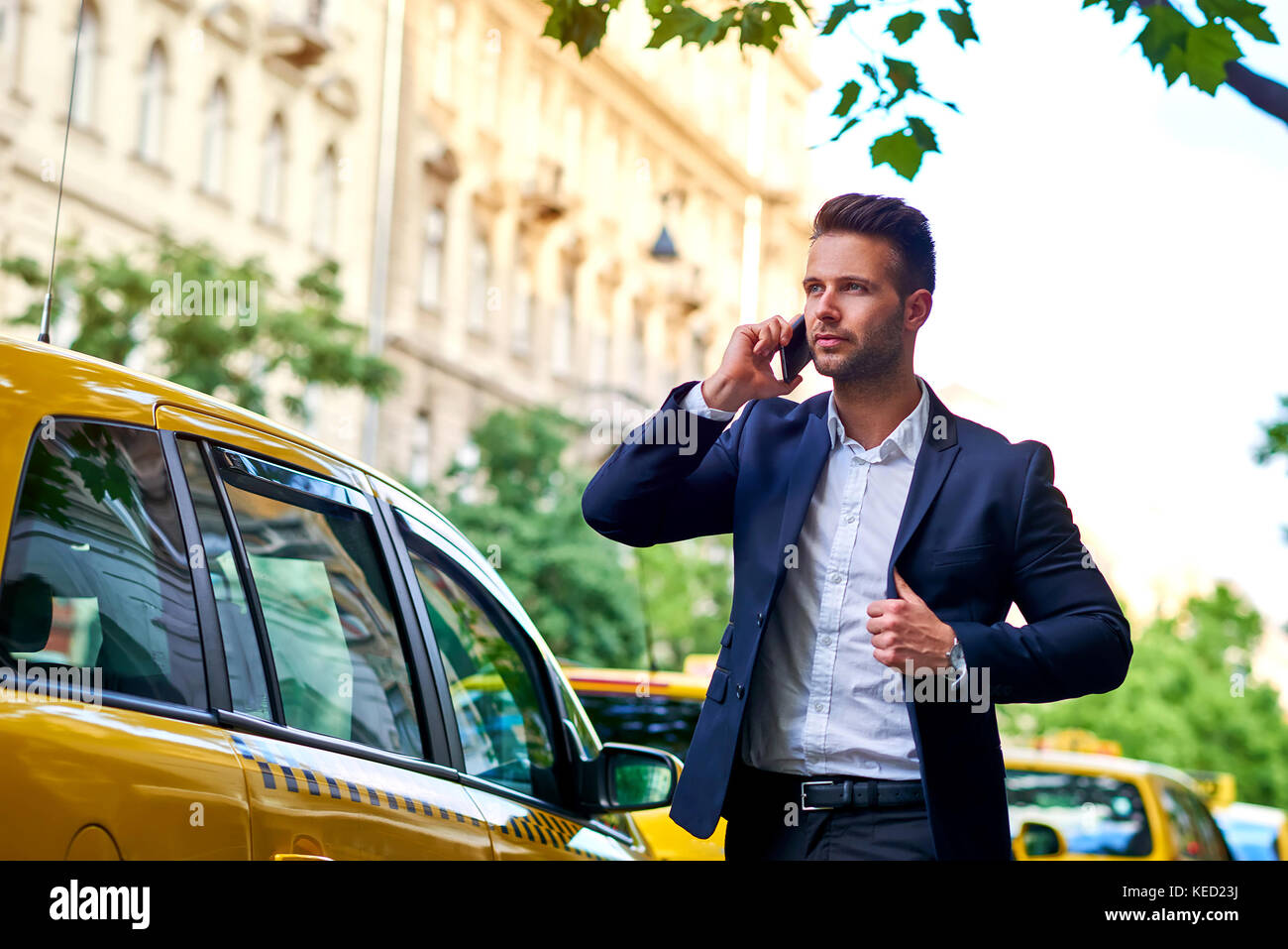 A handsome young businessman waiting for his taxi on the street while ...