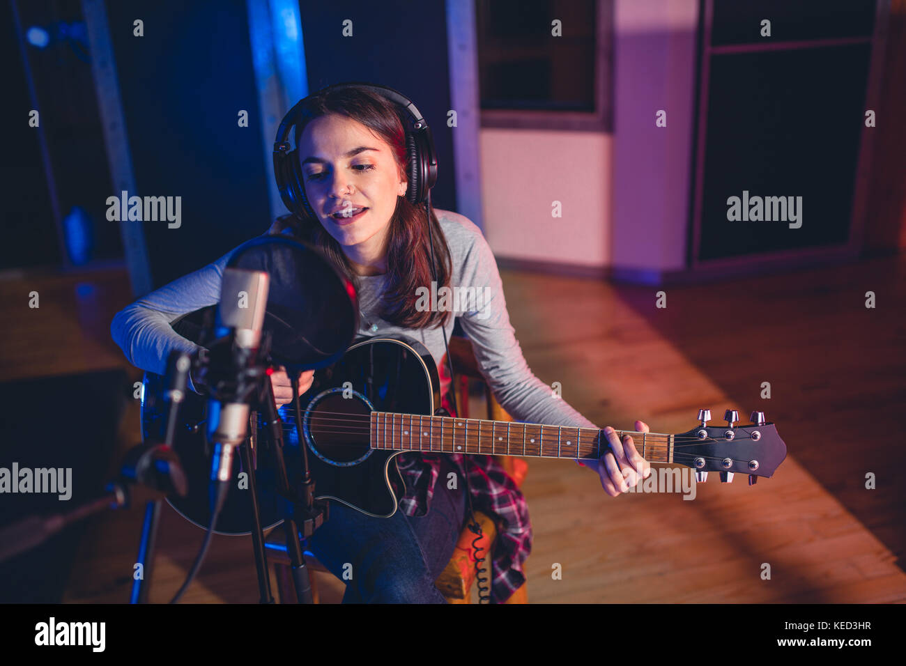 Woman performing in a recording studio. Female singer playing guitar ...