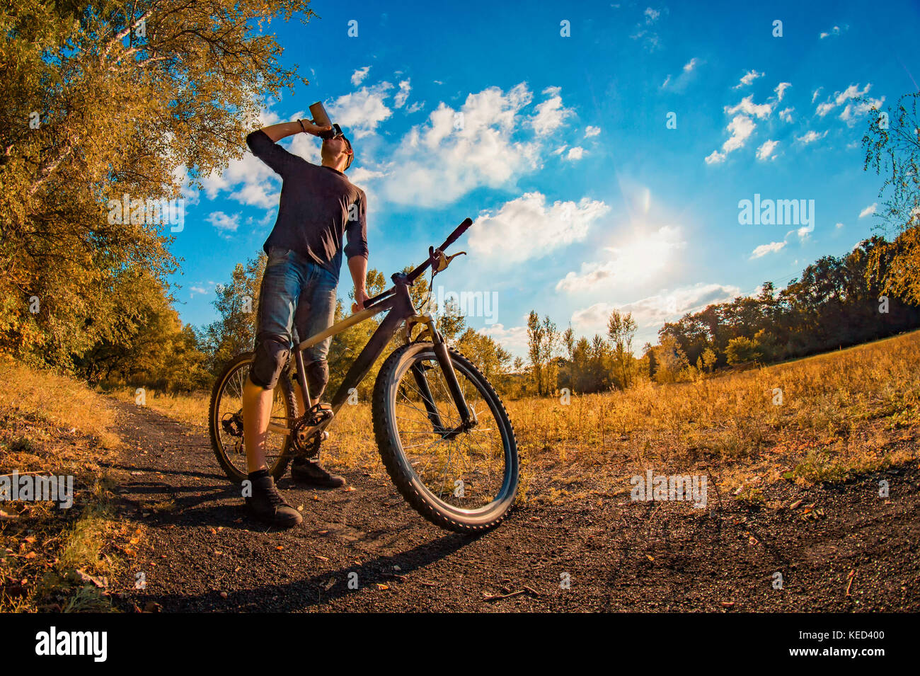 young man drinks a protein shake from a shaker while taking a bike ...