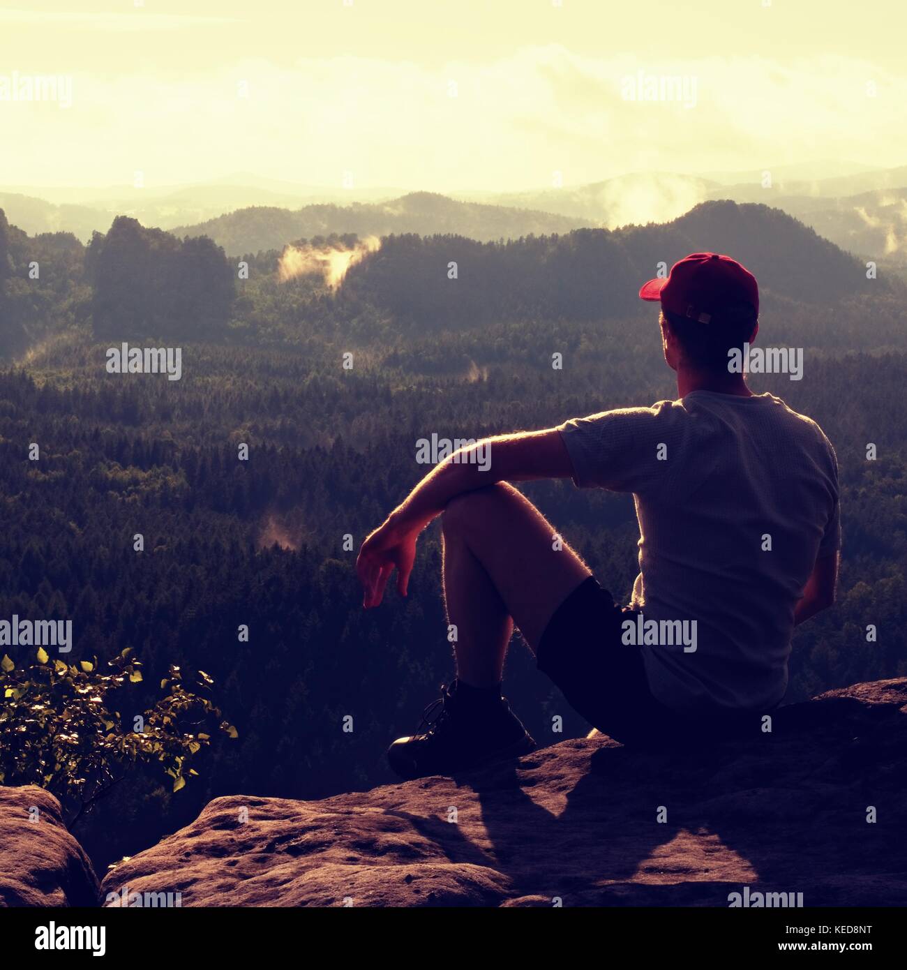 Man tourist sit on exposed rock. View point with sharp rock above misty ...