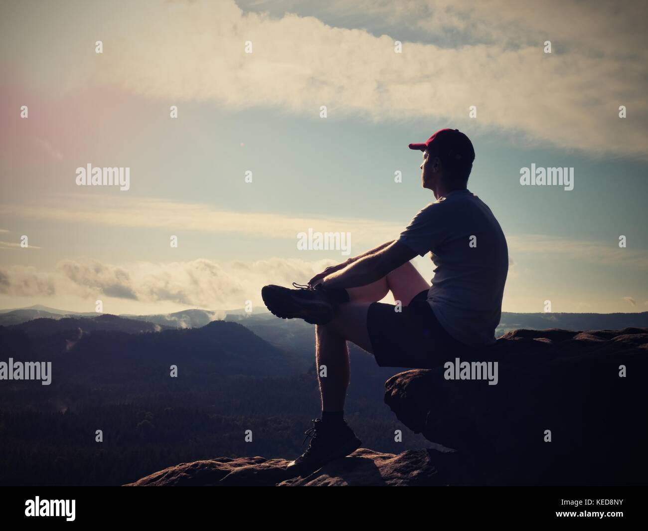 Man tourist sit on exposed rock. View point with sharp rock above misty ...