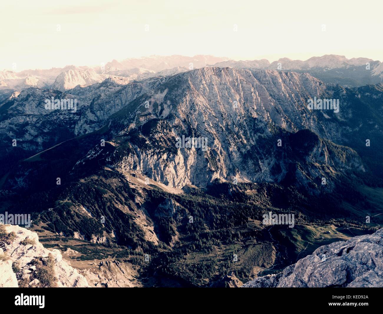 View over Alpine cliff and valley. Sun at horizon, blue sky with few ...