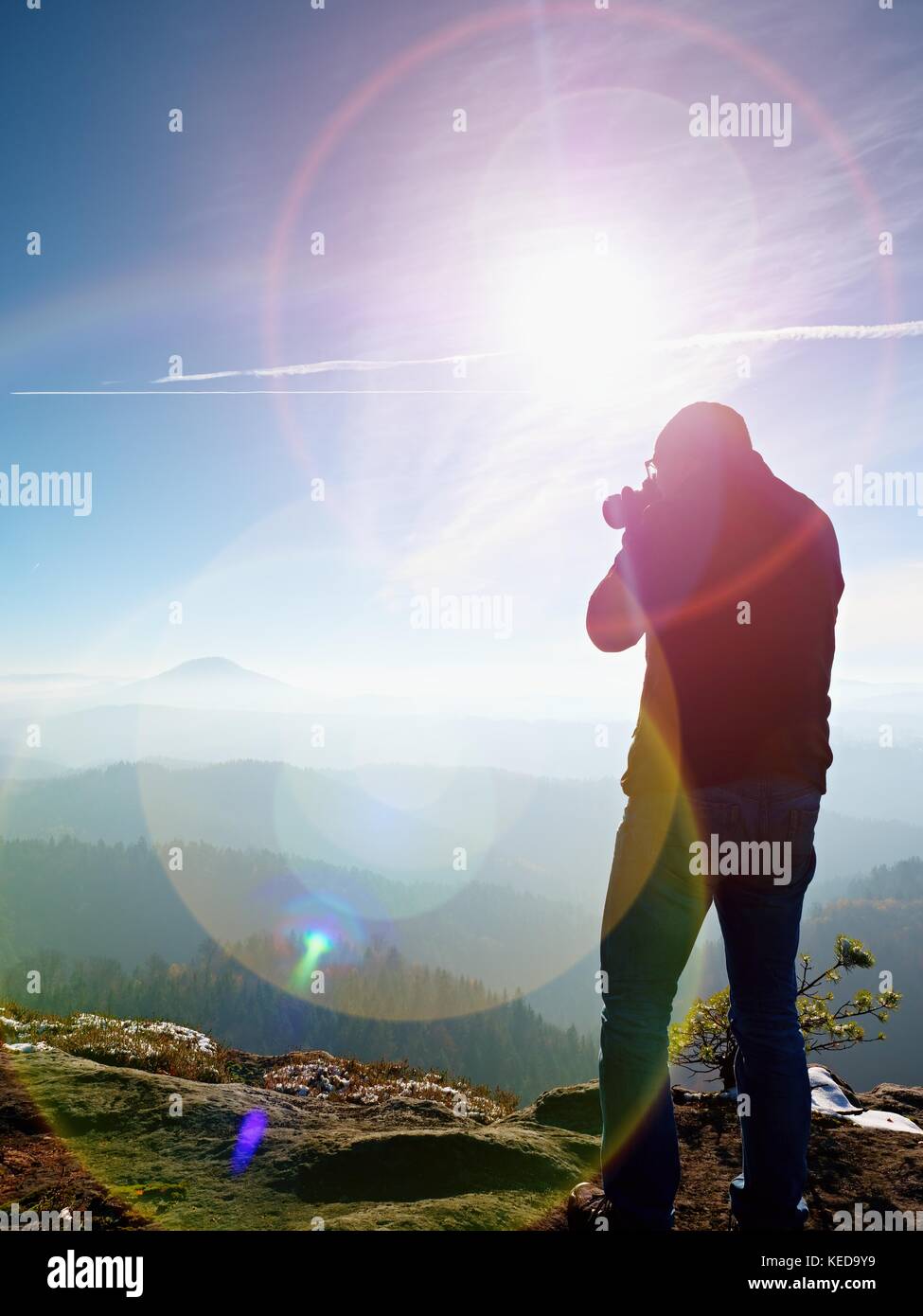 Tall man is taking photo by mirror camera on neck. Snowy rocky peak of ...