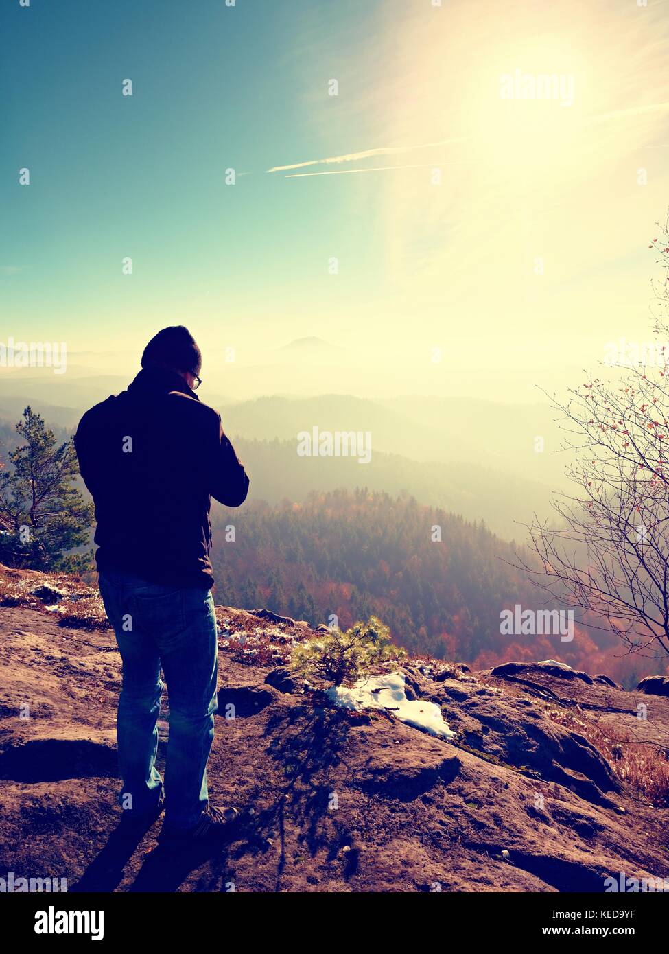Tall man is taking photo by mirror camera on neck. Snowy rocky peak of ...