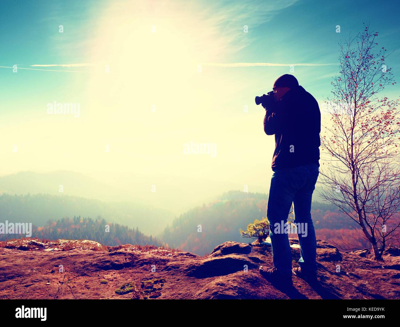 Tall man is taking photo by mirror camera on neck. Snowy rocky peak of ...