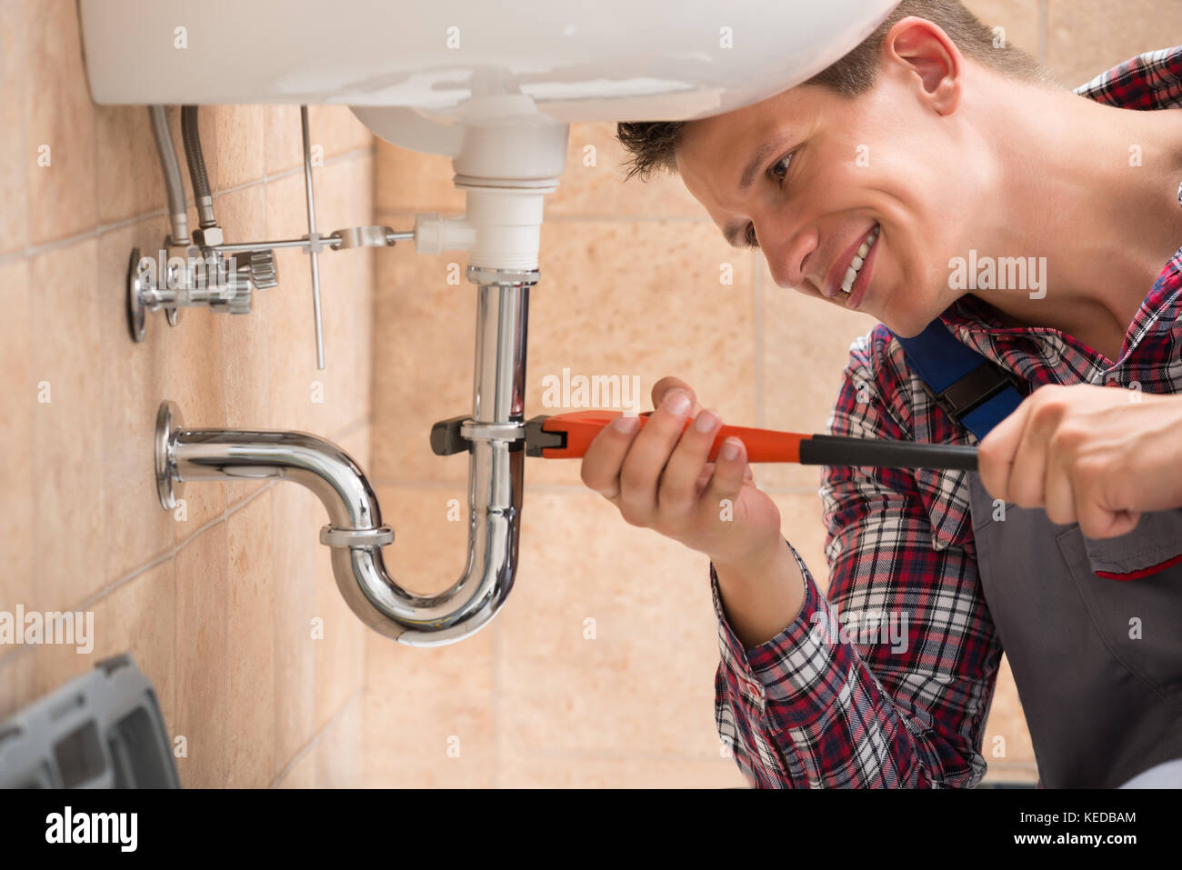 Smiling Male Plumber Fixing Sink Pipe With Adjustable Wrench In ...
