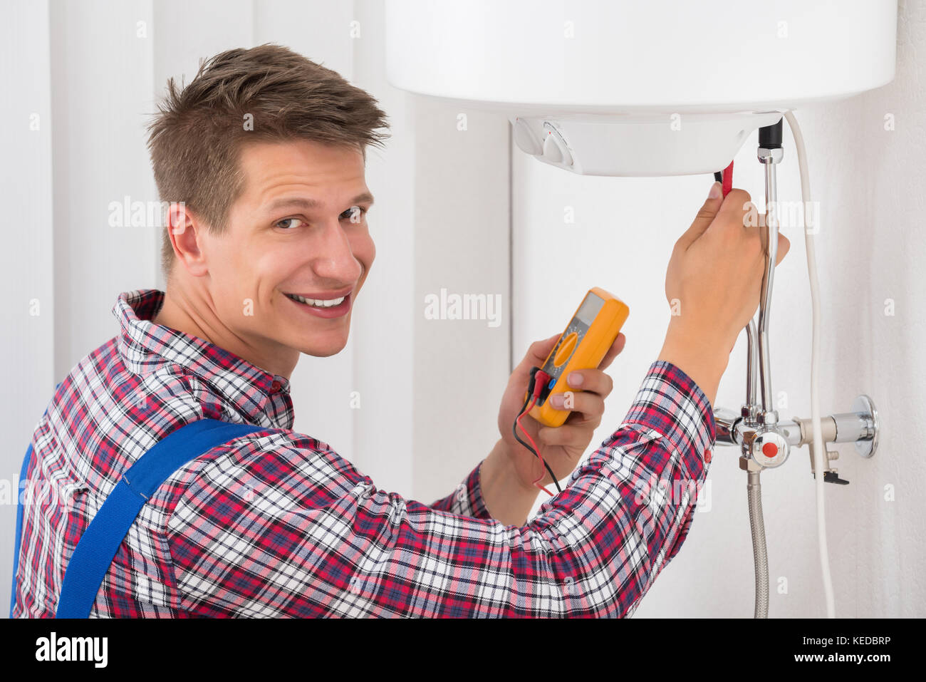 Smiling Male Plumber Examining Electric Boiler With Multimeter Probe ...