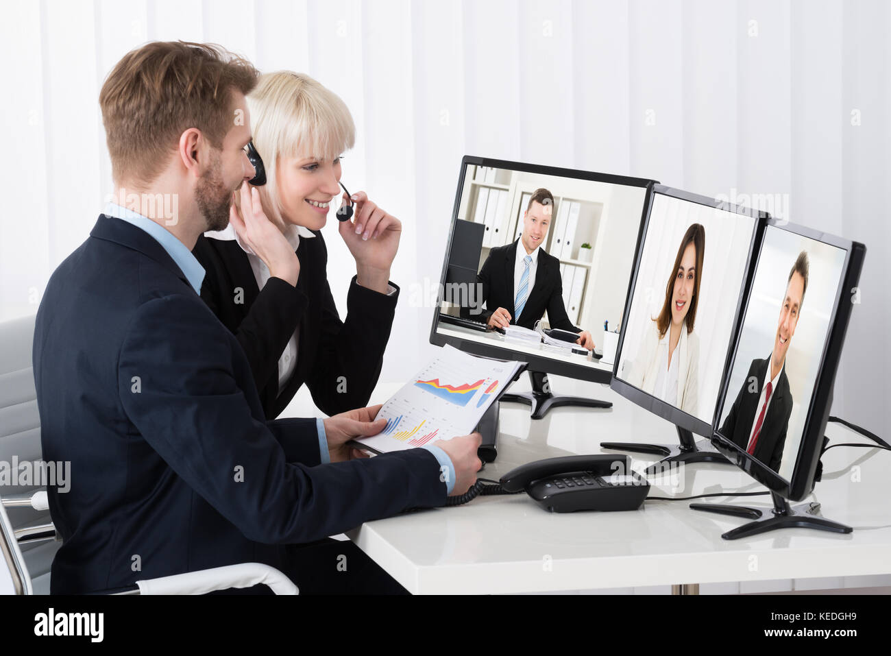 Two Businesspeople Video Conferencing On Desk With Multiple Computer ...