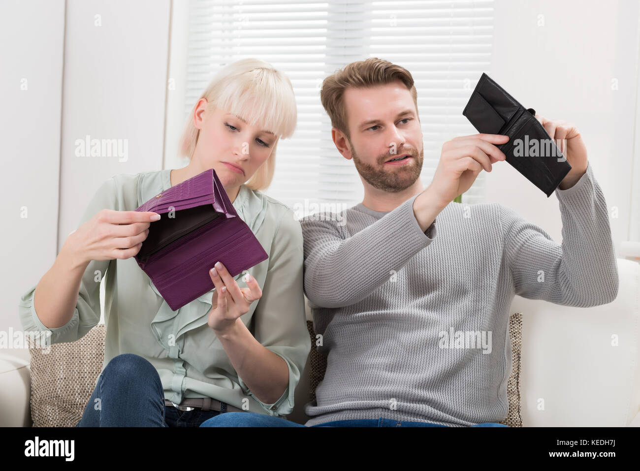 Unhappy Couple Sitting On Sofa Looking At Empty Wallet Stock Photo - Alamy