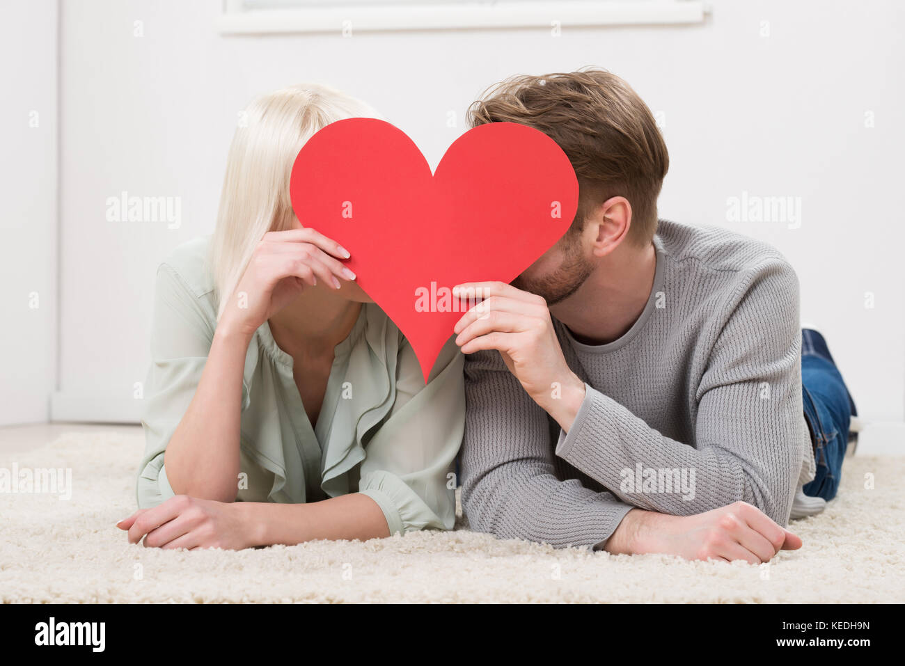 Couple Kissing Behind Heart Shape While Lying On Rug At Home Stock ...