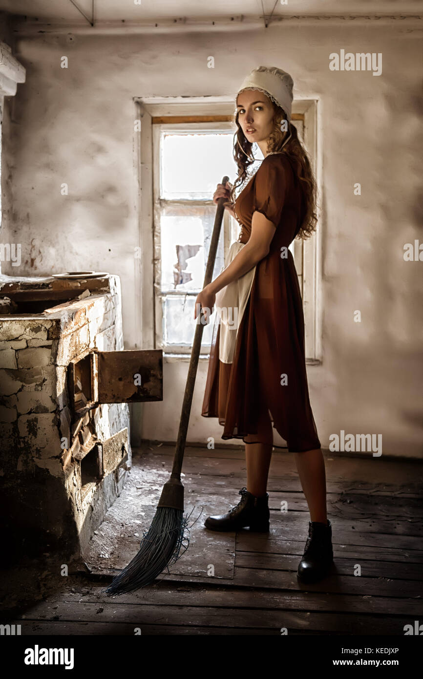woman in a rustic dress sweeps the wooden floor in the kitchen Stock ...