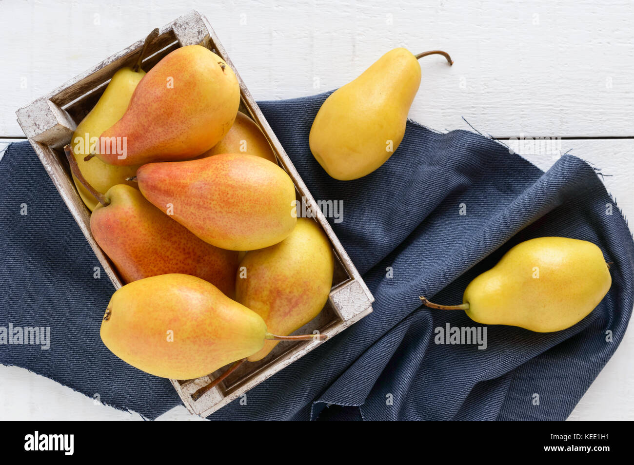 Large juicy yellow pears in a rustic wooden fruit box on a white table ...