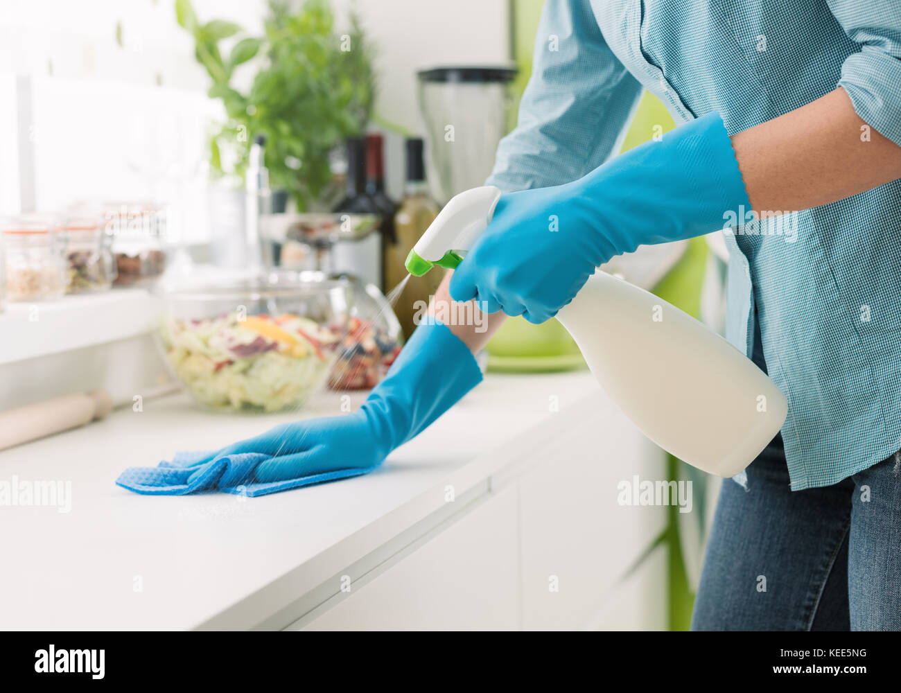 Woman cleaning and polishing the kitchen worktop with a spray detergent ...