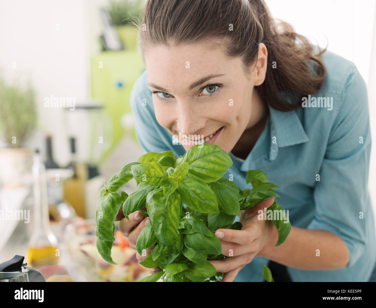 Smiling woman smelling fresh basil at home and preparing healthy food ...