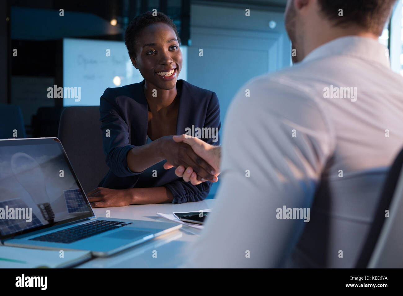 Executives shaking hands at desk in office Stock Photo - Alamy