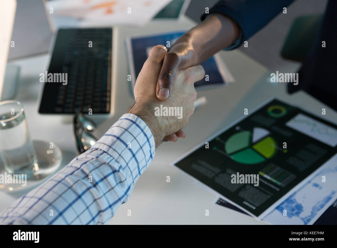 Executives shaking hands at desk in office Stock Photo - Alamy