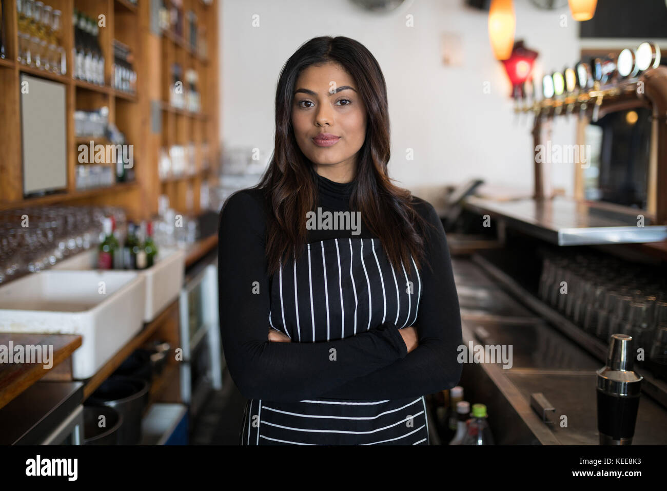 Portrait of beautiful waitress standing with arms crossed in bar Stock ...