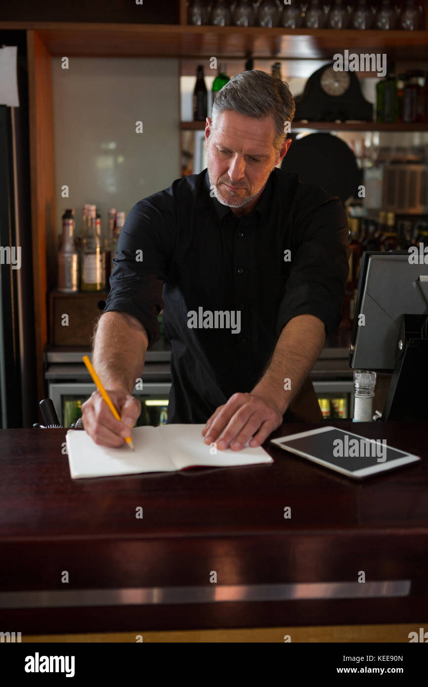 Bar tender writing in a book at bar counter Stock Photo - Alamy