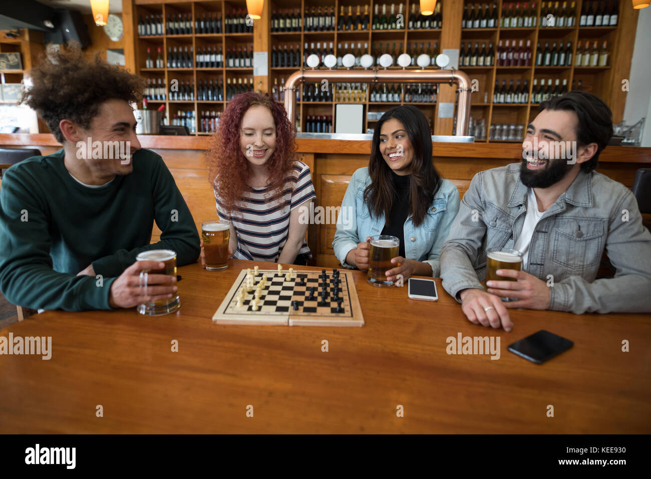 Smiling friends playing chess while having glass of beer in bar Stock ...