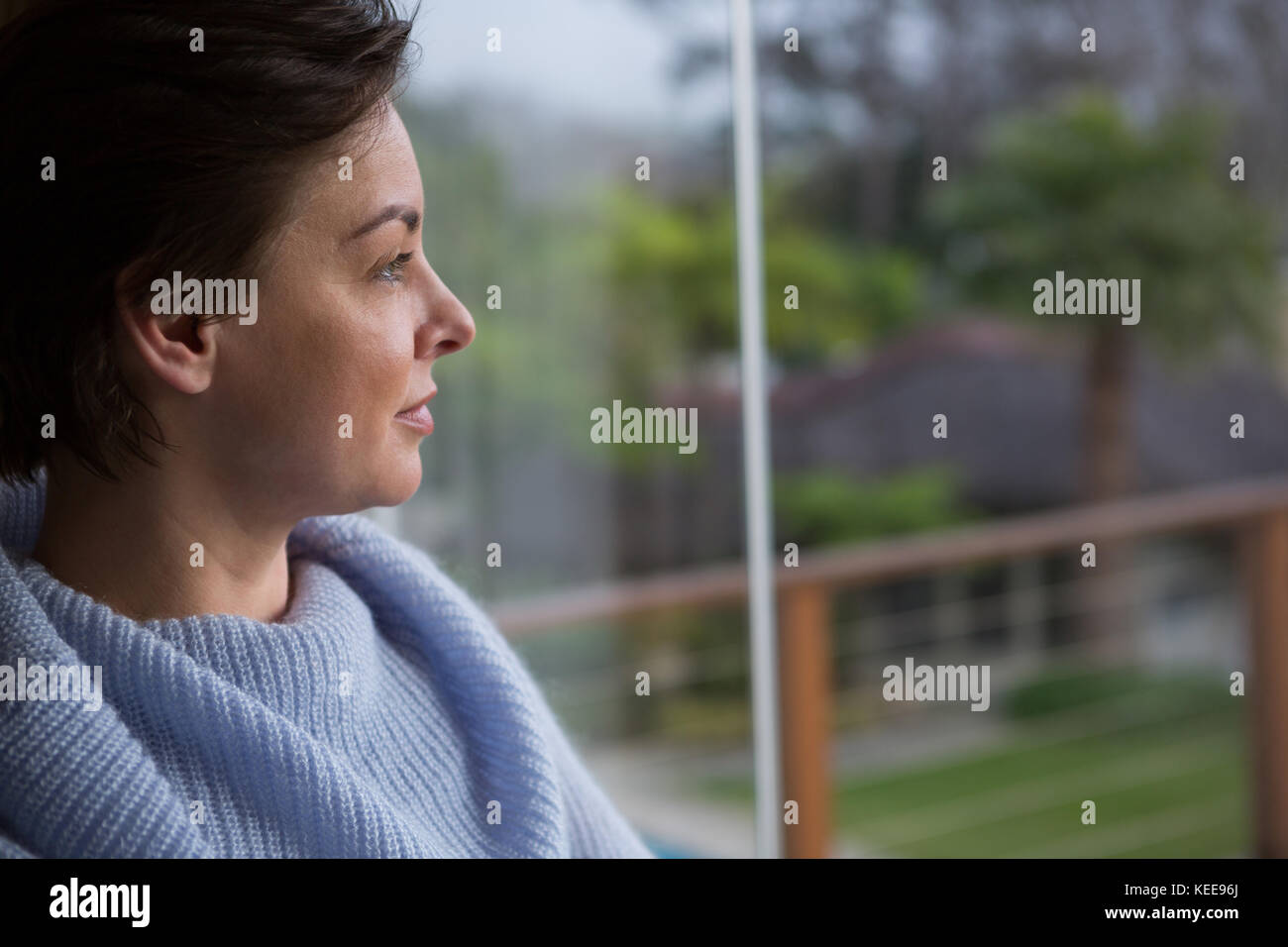 Thoughtful woman looking through window at home Stock Photo - Alamy