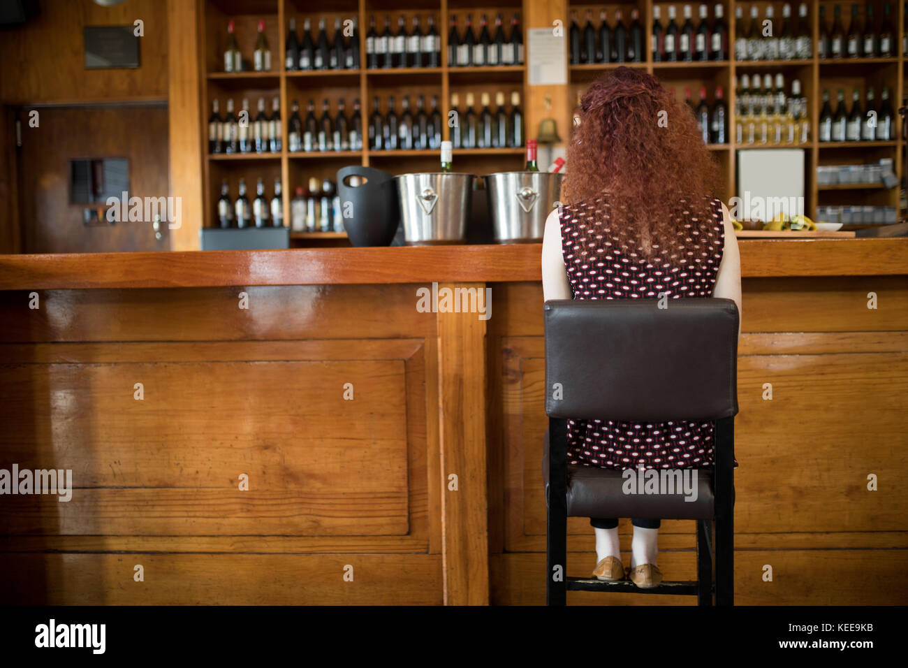 Rear view of woman sitting on chair at counter in bar Stock Photo - Alamy
